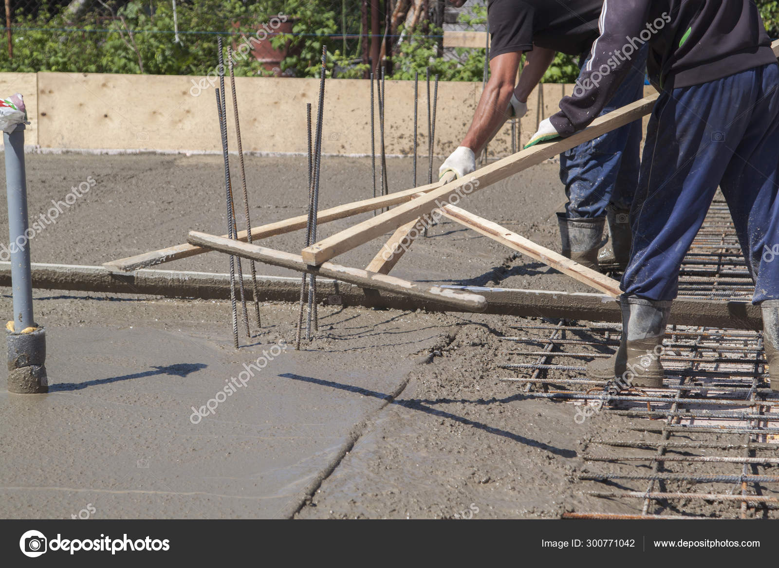 Two workers leveling fresh concrete slab with a special wooden w ...