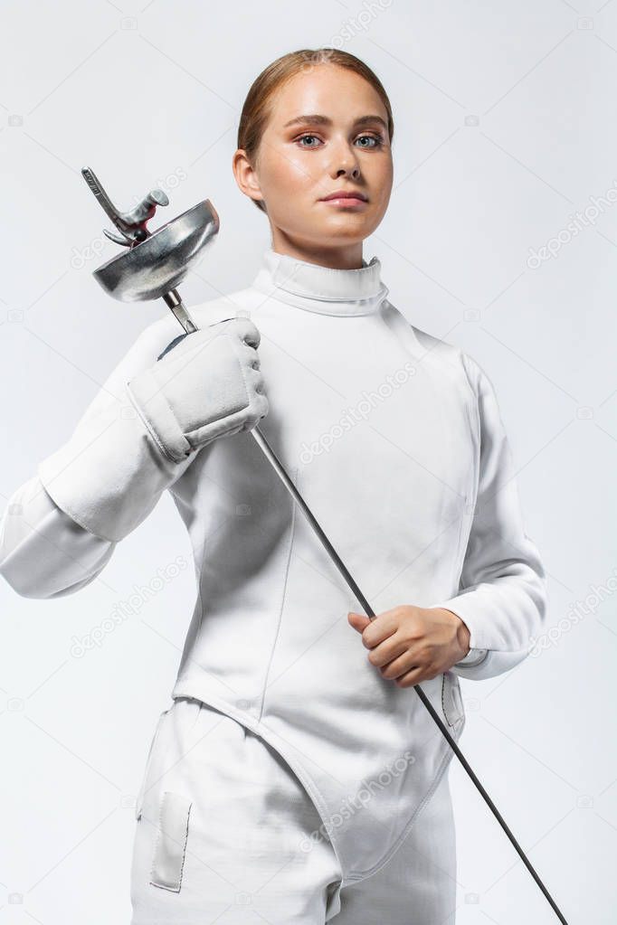 Portrait of Young woman fencer wearing mask and white fencing costume and holding the sword in ...