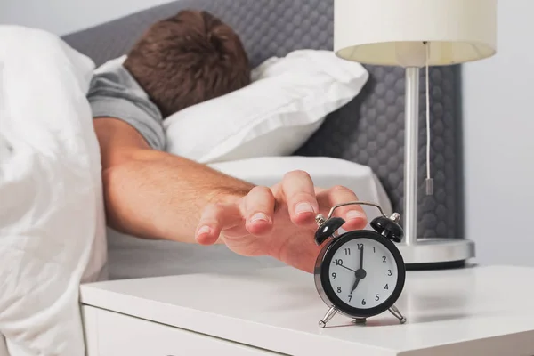 Mans hand reaching out alarm clock on the nightstand early in the ...