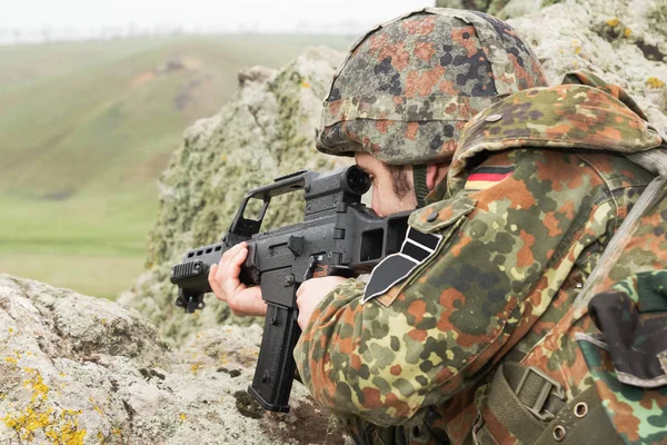 Young white soldier in bulletproof helmet shooting with automatic rifle ...