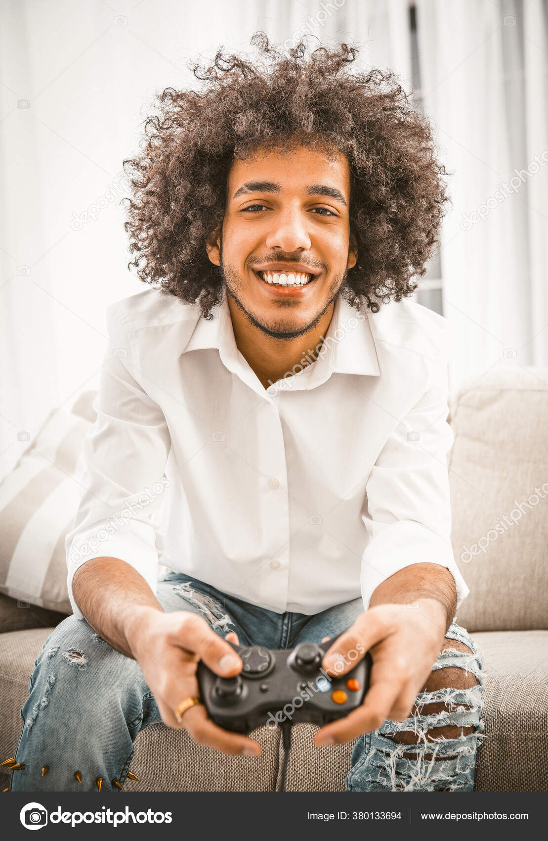 Happy Arab man smiles broadly playing computer game. Shaggy gamer holds ...
