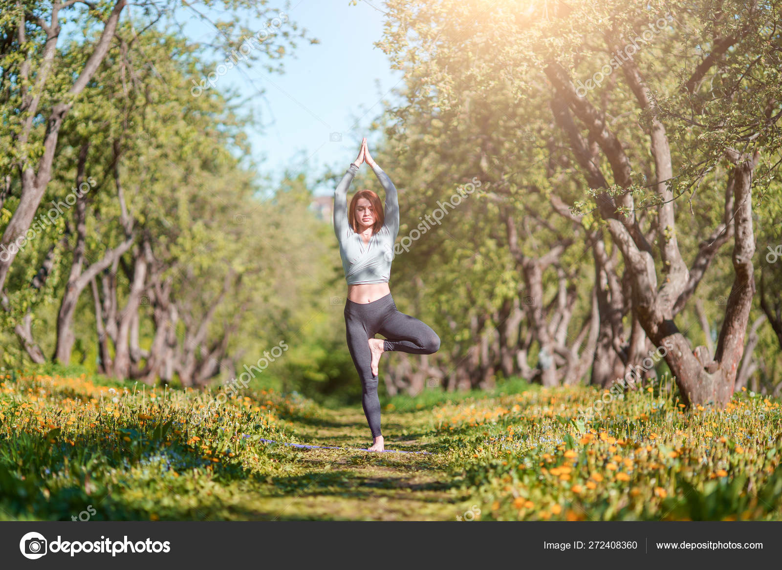 Photo of woman with one arm raised on one leg practicing yoga in forest ...
