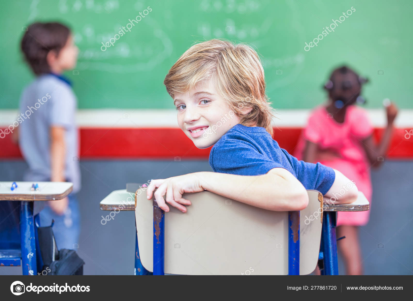 Primary school classroom. Young boy turning back to his classmat ...