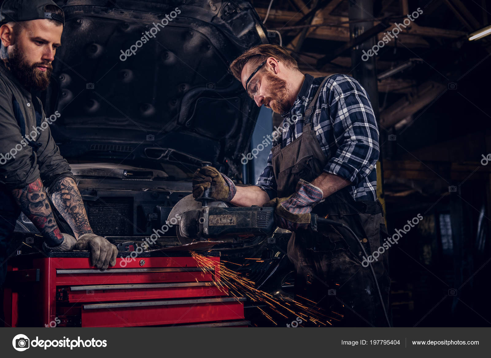 Two bearded auto mechanic in a uniform and safety glasses working with ...