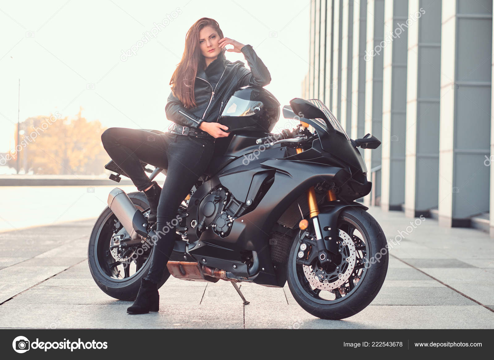 A Beautiful Biker Girl Leaning On Her Superbike Outside A Building