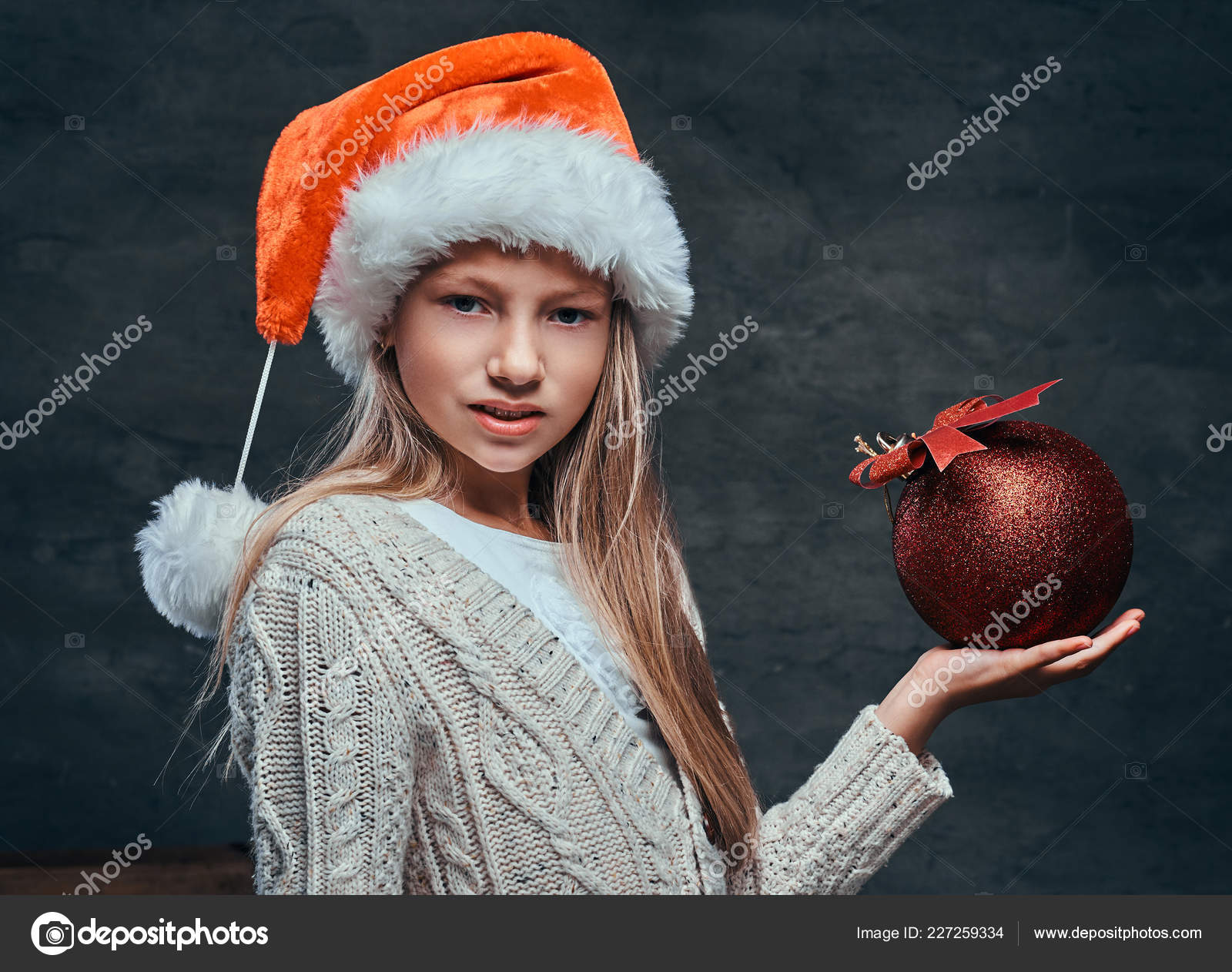 Teen boy wearing Santas hat holding a big Christmas ball on a dark ...