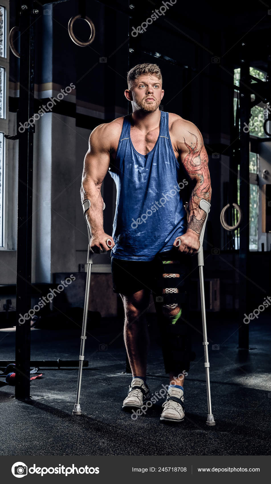 Muscular bodybuilder standing with crutches and bandage on a leg in a ...