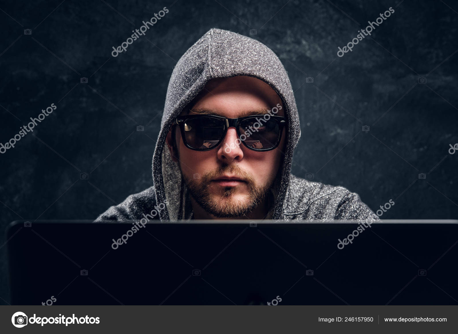 Close-up portrait of a hacker in hoodie and sunglasses sits behind ...