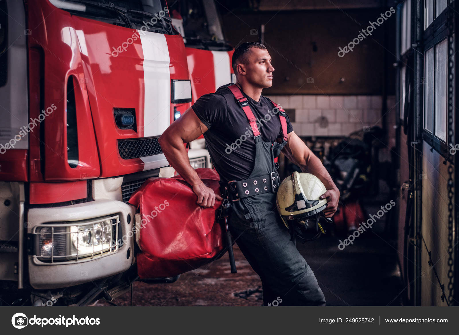 Muscular fireman holding a protective helmet in a garage of a fire ...