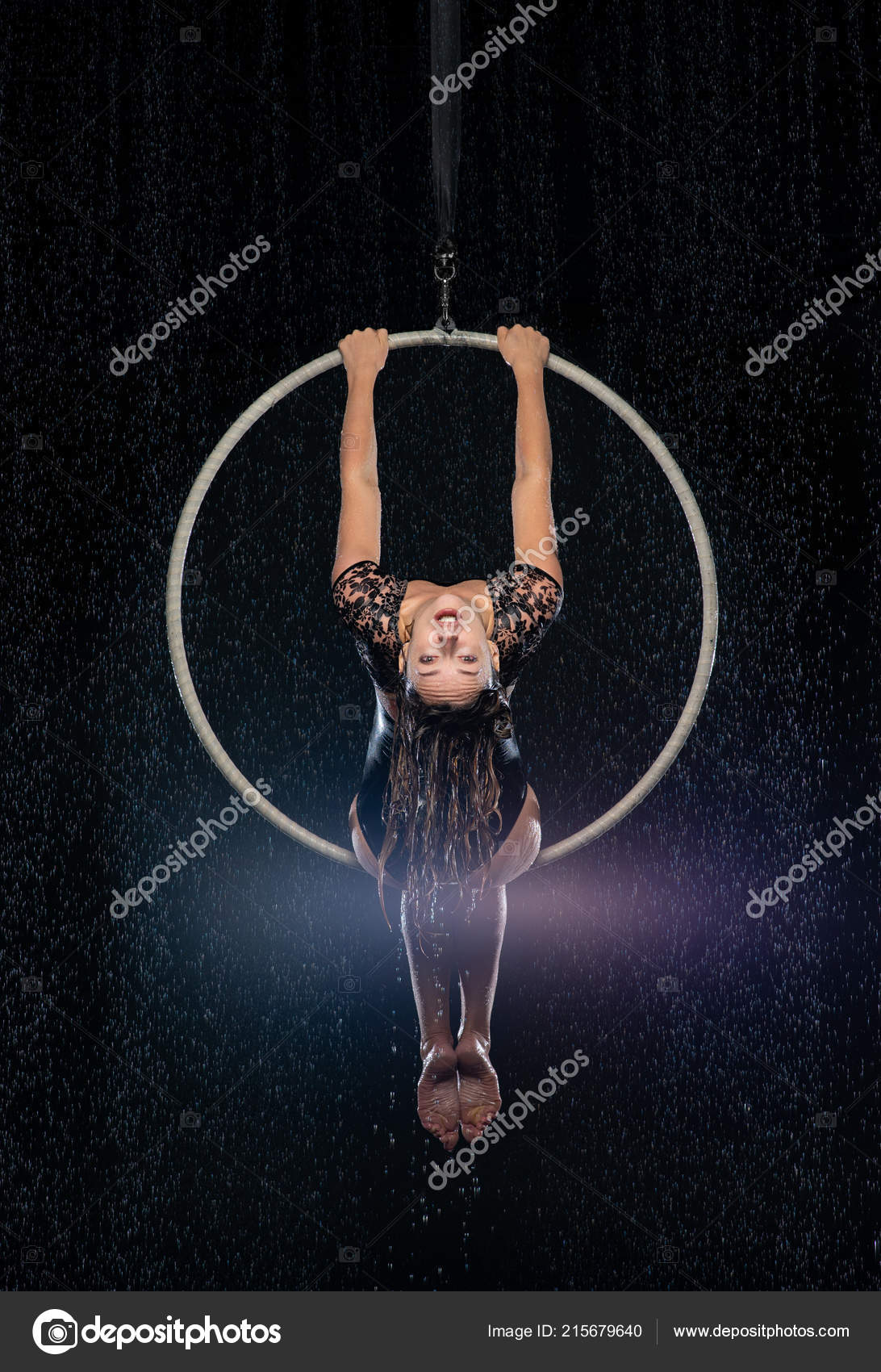 Beautiful female acrobat sitting on symmetric pose in aerial hoop under ...