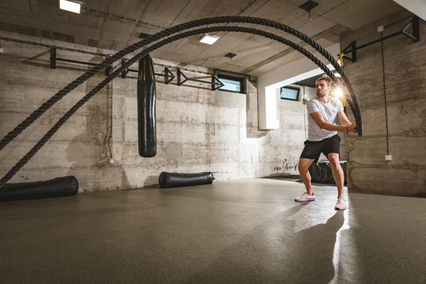 Young man doing strength training using heavy ropes at gym - Stock ...