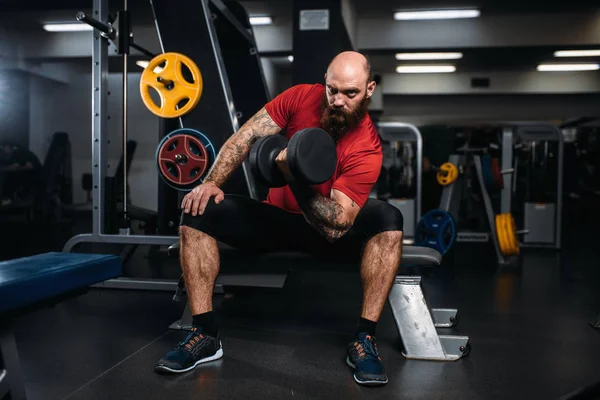 Strong athlete with dumbbell in action, workout in gym. Bearded ...