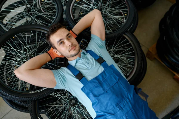 Male worker lying on stack of bicycle wheels on factory. Bike rims assembly line in workshop ...