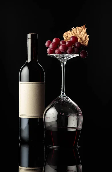 Bottle of red wine and an inverted wine glass with wine on a black ...