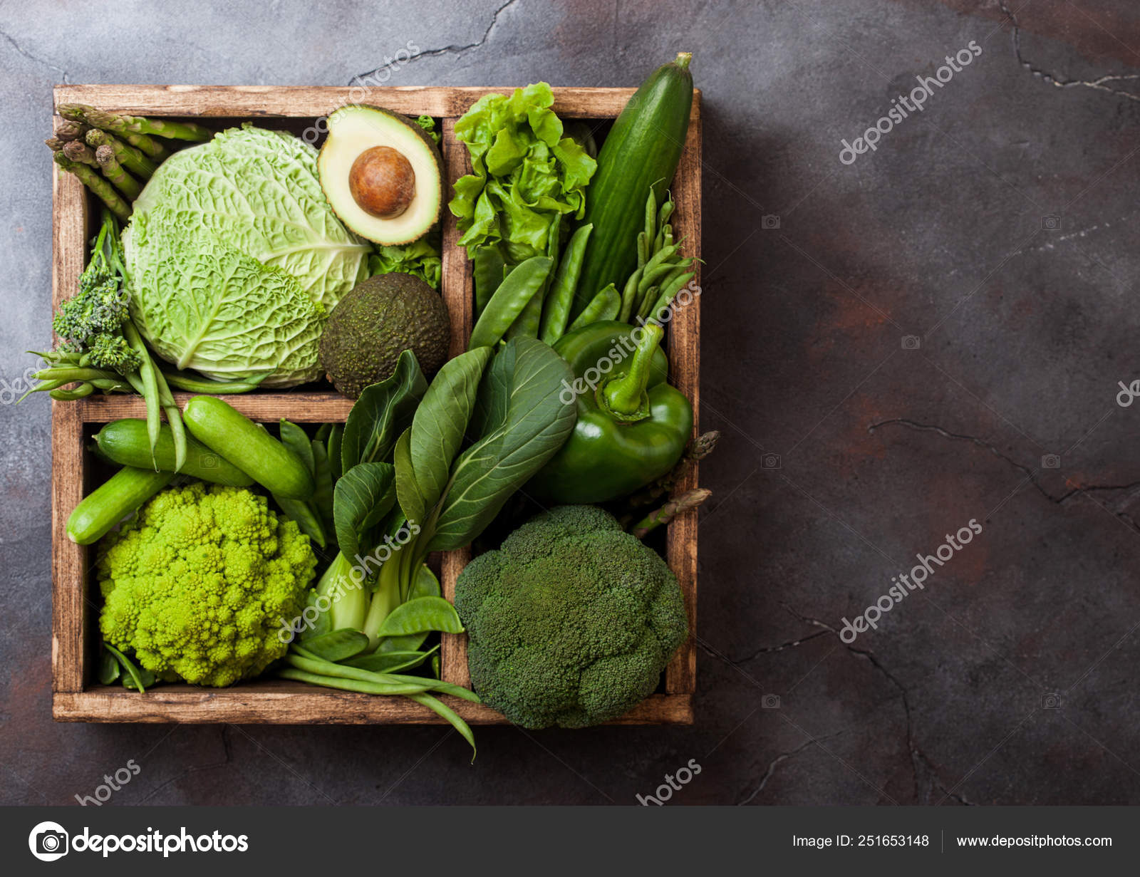 Assorted green toned raw organic vegetables in wooden box on dark ...