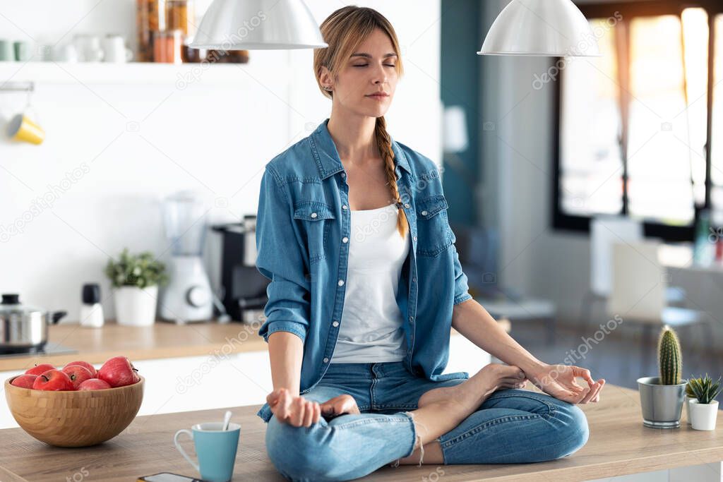 Foto de mujer joven y bonita en posición de loto sentada en la mesa mientras se relaja en la ...