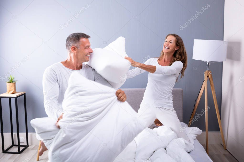 Pareja feliz luchando juntos con almohadas blancas en la cama 2023