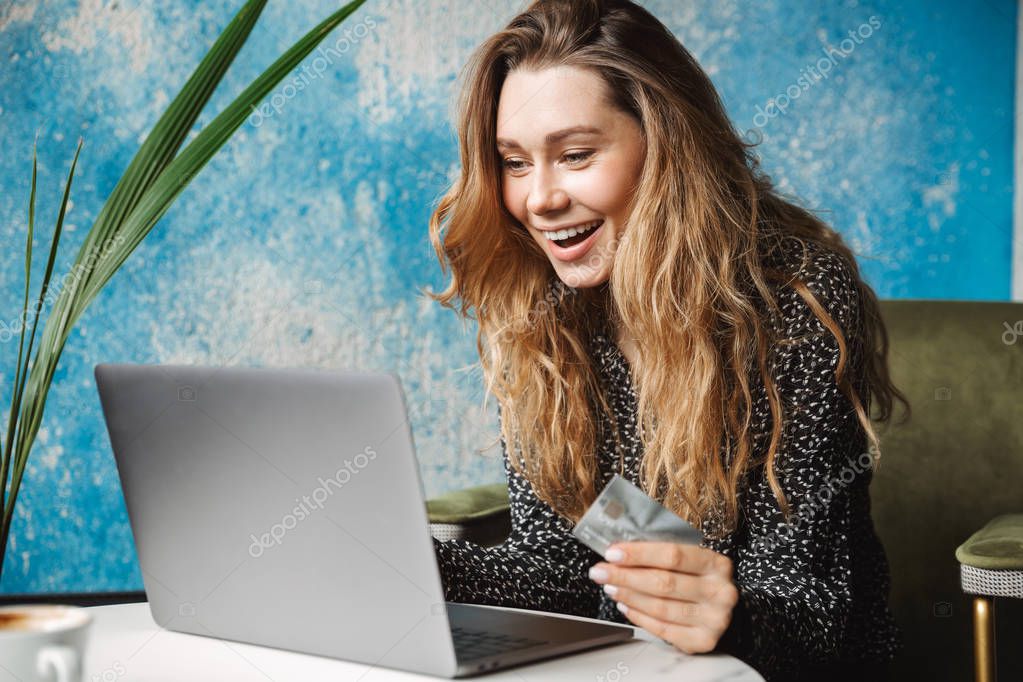 Imagen de una hermosa mujer joven y bonita sentada en un caf en el interior usando una ...