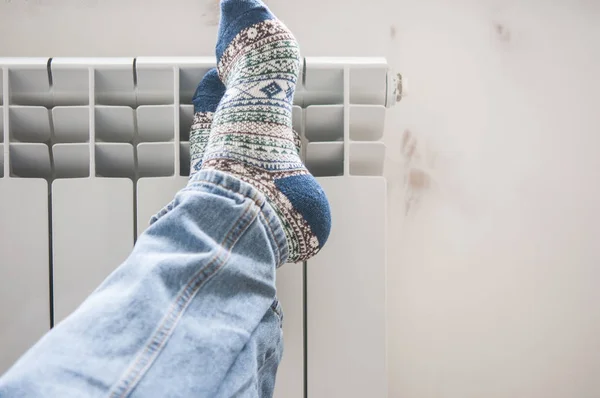 Man warming legs on heating radiator near white wall - Stock Image ...