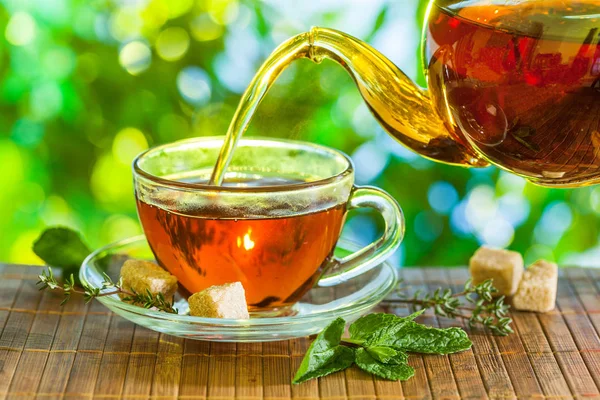 Tea time. Pouring out hot tea into a cup. Green nature background ...