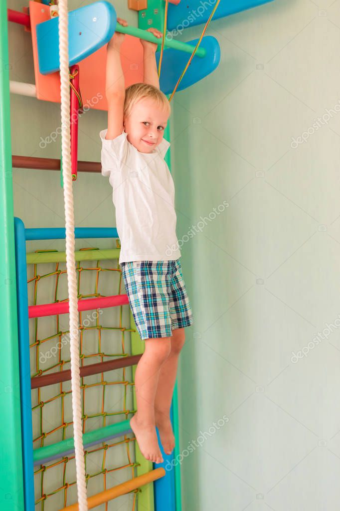 Niño feliz colgando de anillos en el gimnasio de la pared del hogar ...