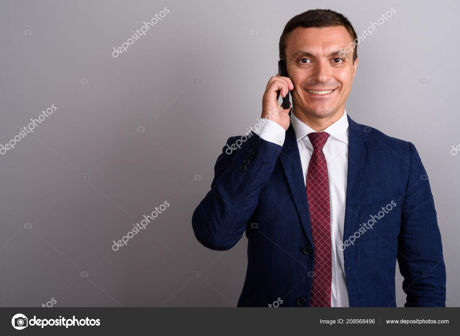 Businessman wearing suit while using mobile phone against gray b Stock ...