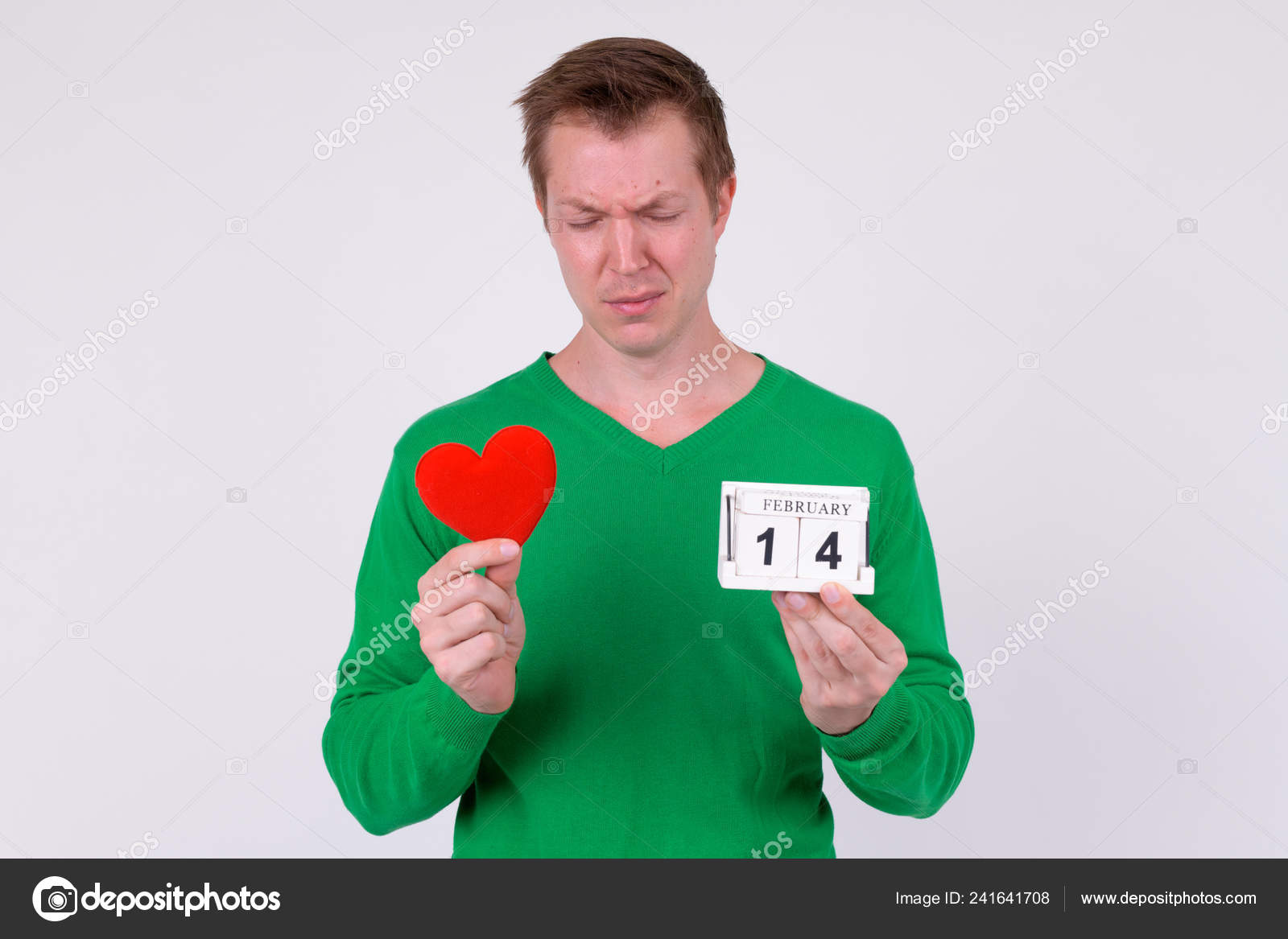 Sad young man holding calendar block and heart ready for Valentines day ...