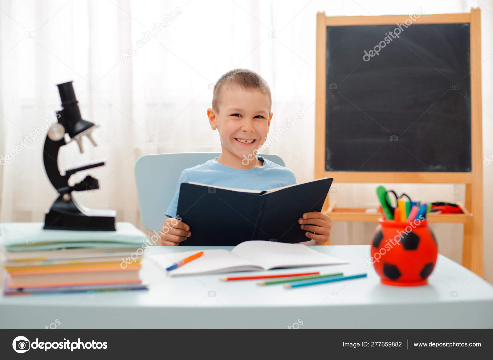 School boy sitting at home classroom lying desk filled with books ...