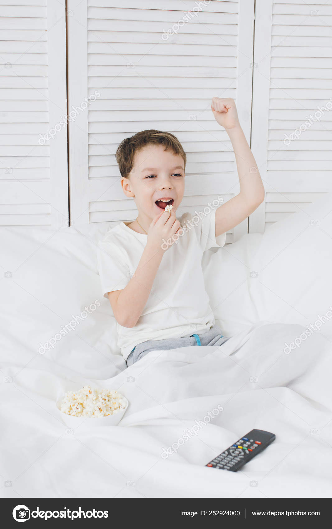 Boy eating popcorn sitting in bed and watching TV — Stock Photo ...