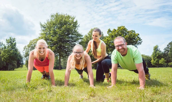 Family doing push-ups in nature under guidance by a fitness coach ...