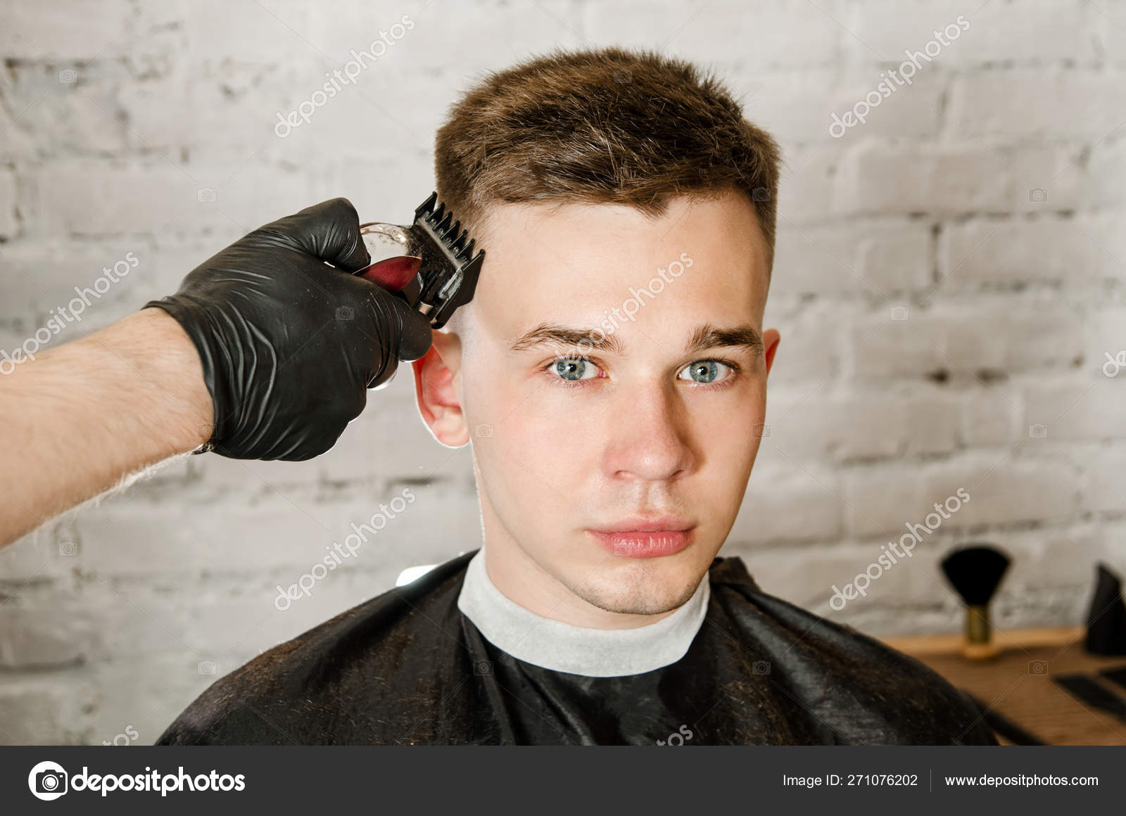 Barber hand in gloves cut hair and shaves young man on a brick wall ...