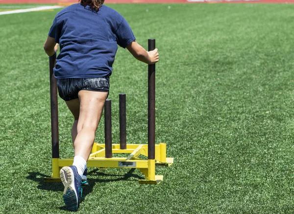 A high school track and field runner is pushing a yellow sled on a ...