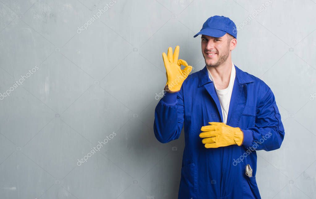 Joven caucásico hombre sobre gris grunge pared usando mecánico uniforme ...