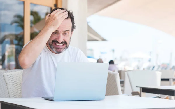 Handsome senior man using laptop at restaurant stressed with hand on ...