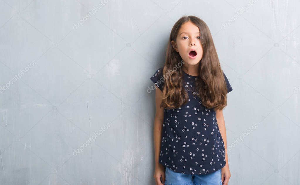 Niño hispano joven sobre la pared gris grunge asustado y sorprendido ...