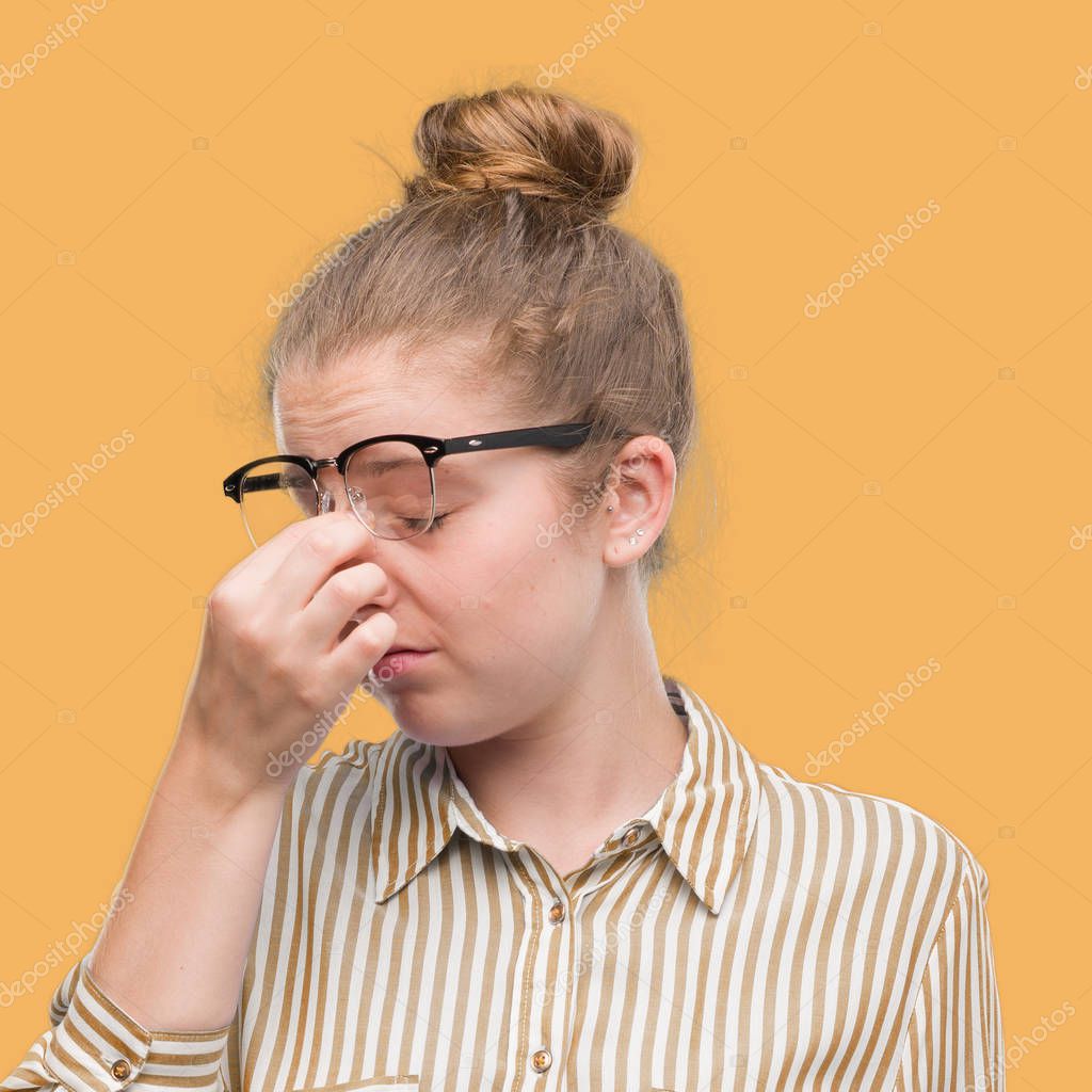 Joven mujer de negocios rubia cansada frotando la nariz y los ojos sintiendo fatiga y dolor de ...