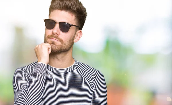Young handsome man wearing sunglasses with hand on chin thinking about ...