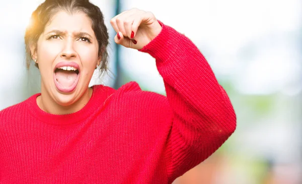 Young beautiful woman wearing red sweater and bun angry and mad raising ...