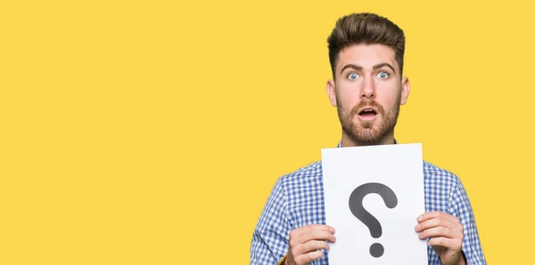 Young handsome man holding paper with question mark scared in shock ...