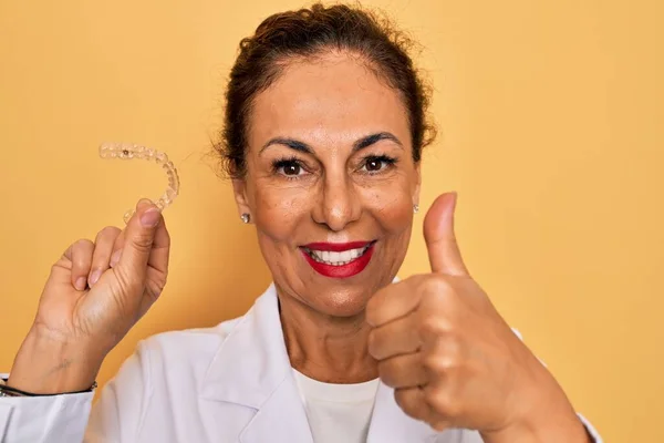 Middle age senior dentist woman holding clear aligner for teeth ...