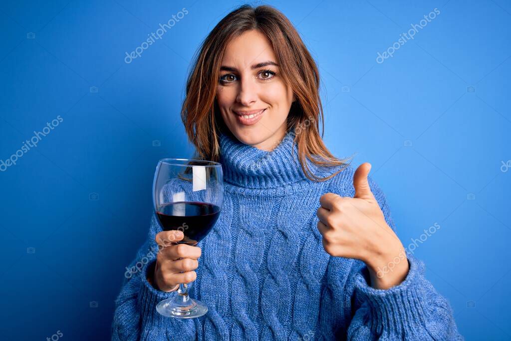 Joven hermosa morena bebiendo copa de vino tinto sobre fondo azul ...