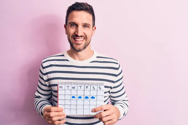 Young handsome man holding weather calendar showing rainy week over ...