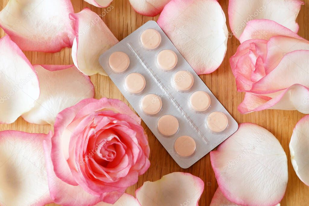 píldoras en ampolla y rosas rosadas con pétalos sobre fondo de madera ...