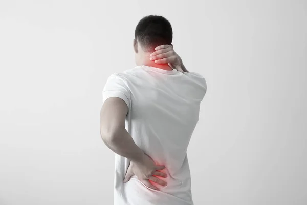 Young man suffering from back pain on light background - Stock Image ...