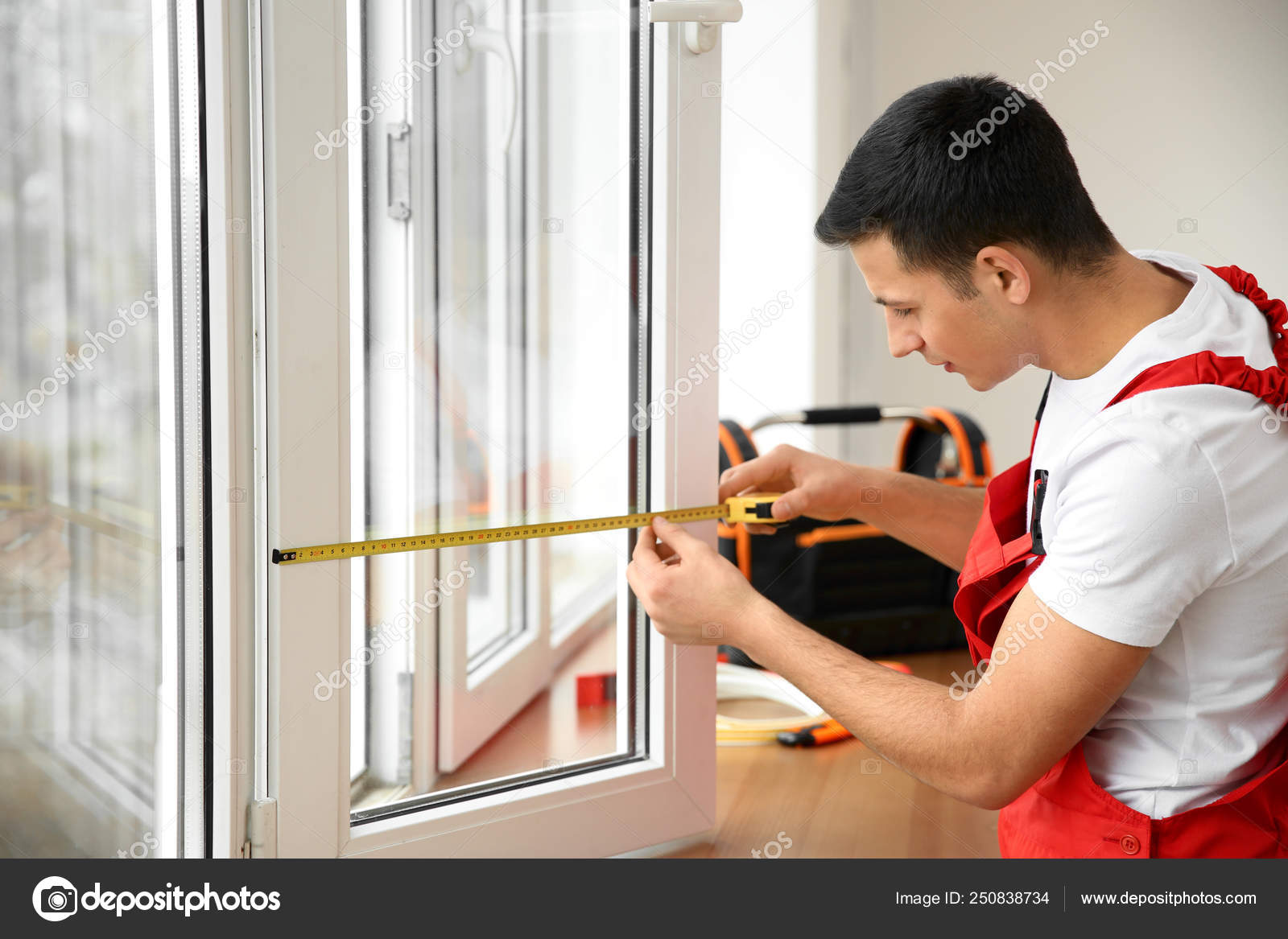 Young worker taking measurements of window in flat Stock Photo by ...