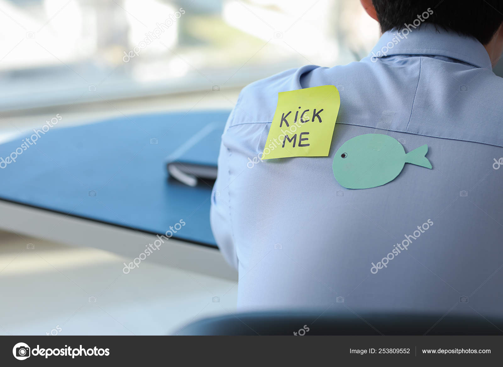 Sticky note with text KICK ME and paper fish on back of man working in ...