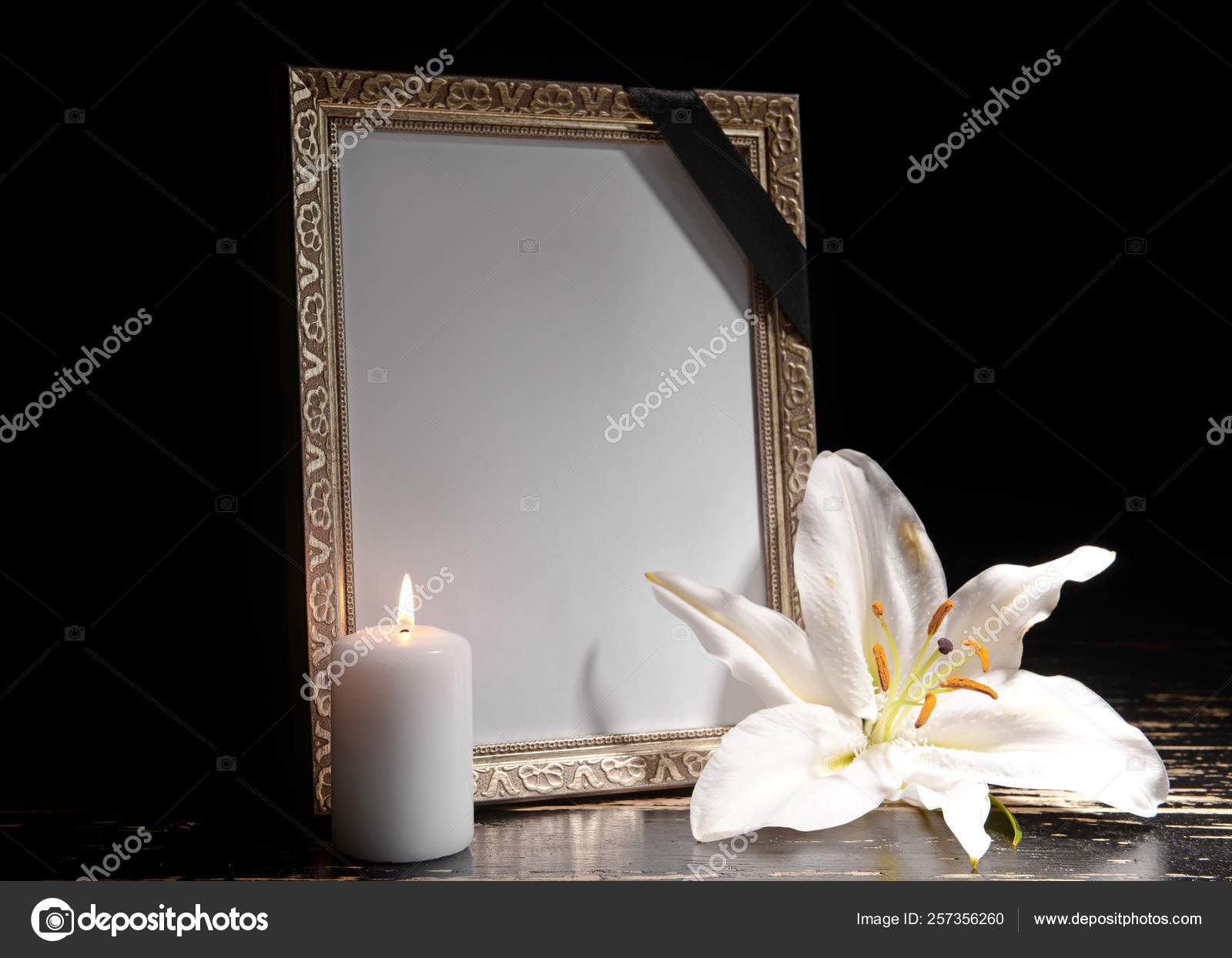Blank funeral frame, burning candle and flower on table against dark ...