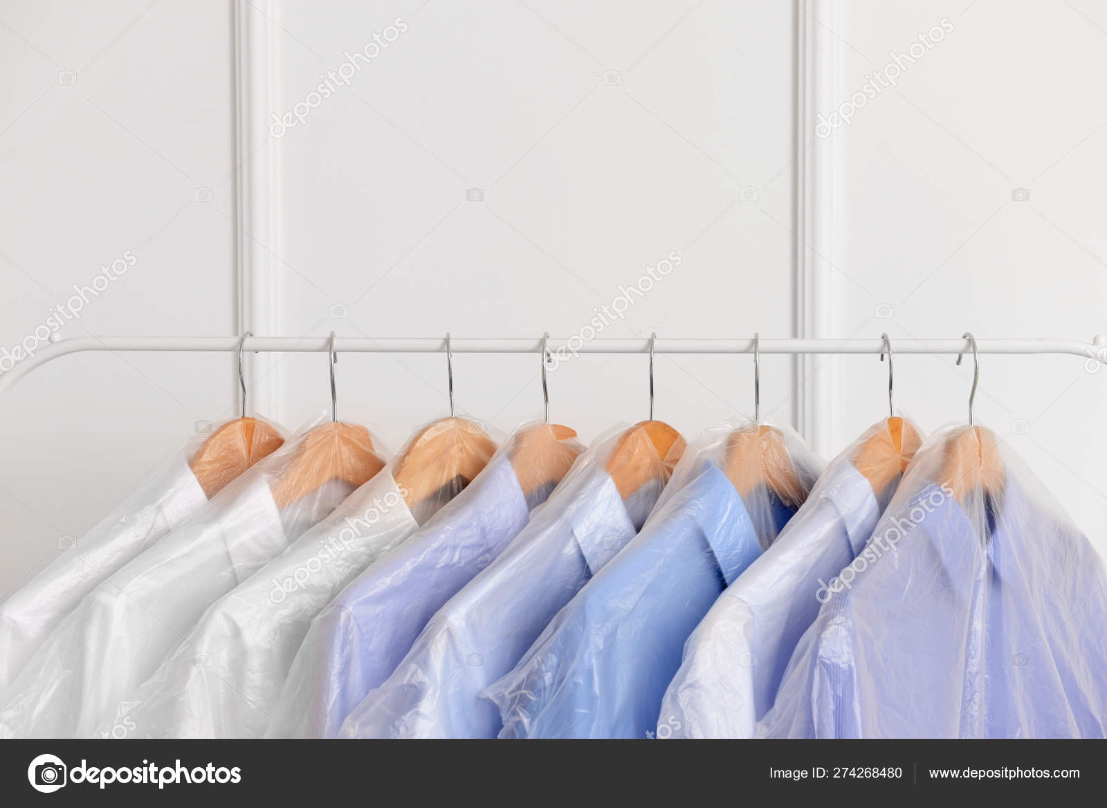 Rack with clothes after dry-cleaning near white wall Stock Photo by ...