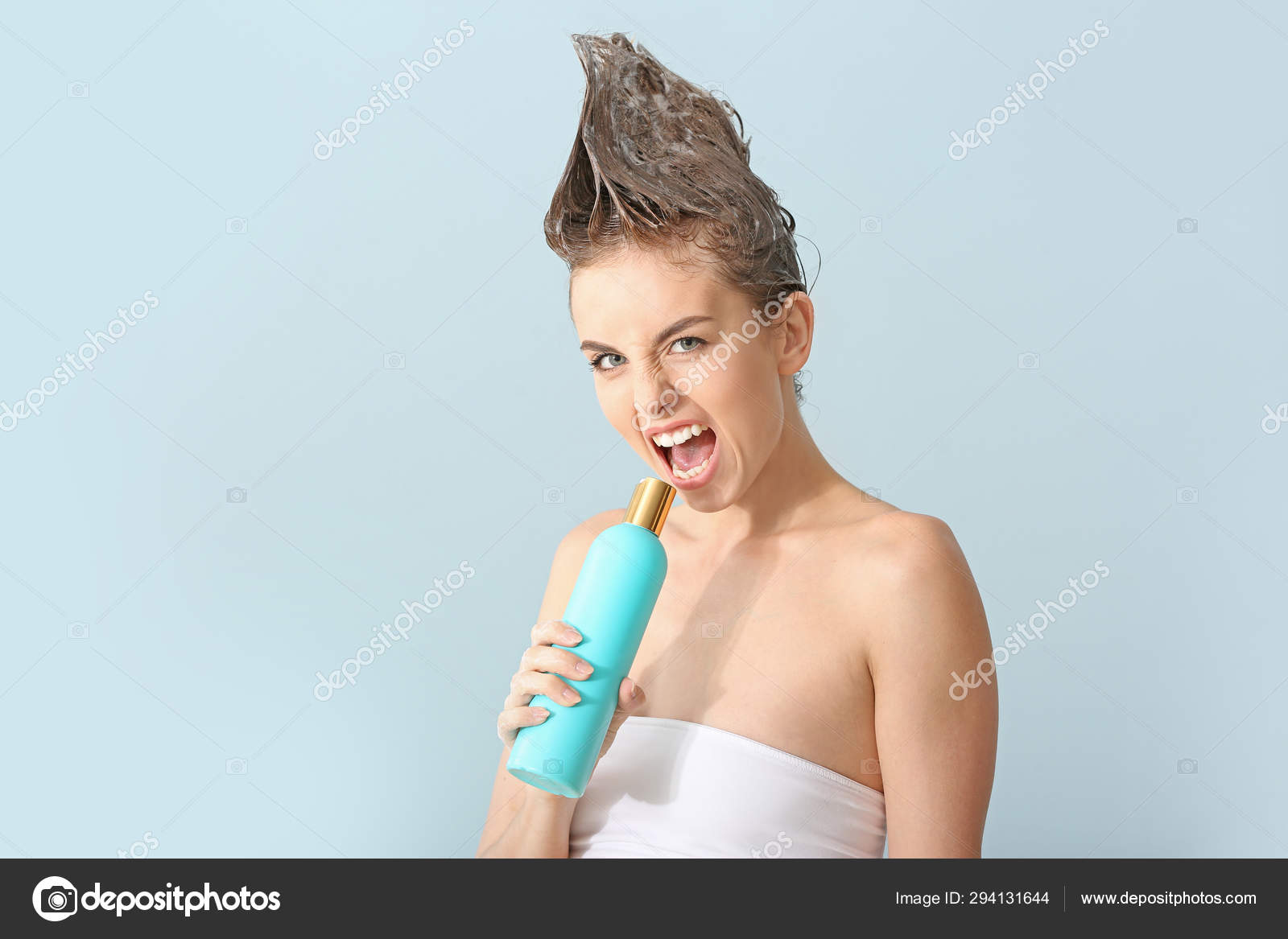 Beautiful young woman using bottle of shampoo as microphone against ...