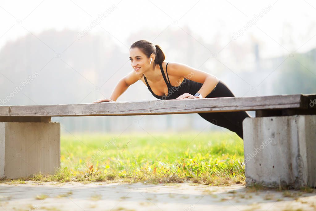 Estilo de vida saludable. Mujer deportiva haciendo ejercicios en el banco y escuchando música en ...